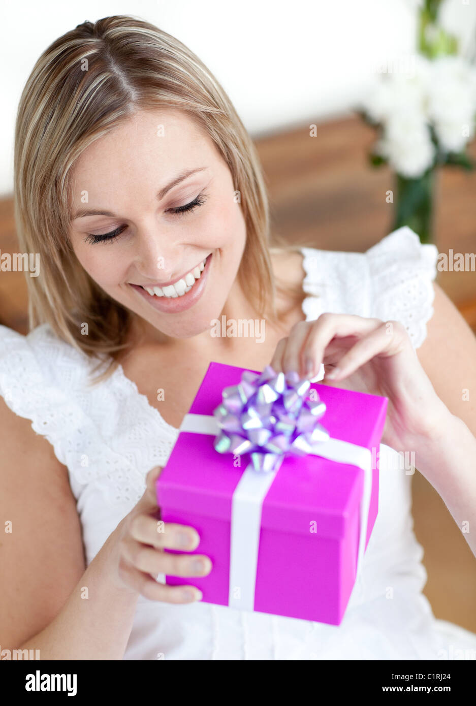 Delighted woman opening a gift sitting on the floor Stock Photo - Alamy