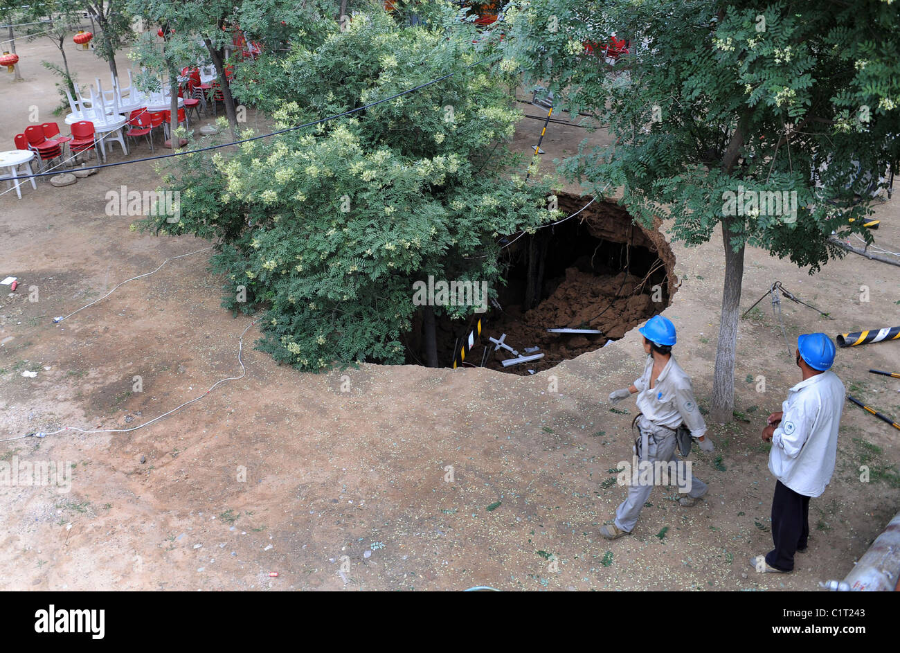 Workers try to salvage a huge tree which has disappeared into a hole ...