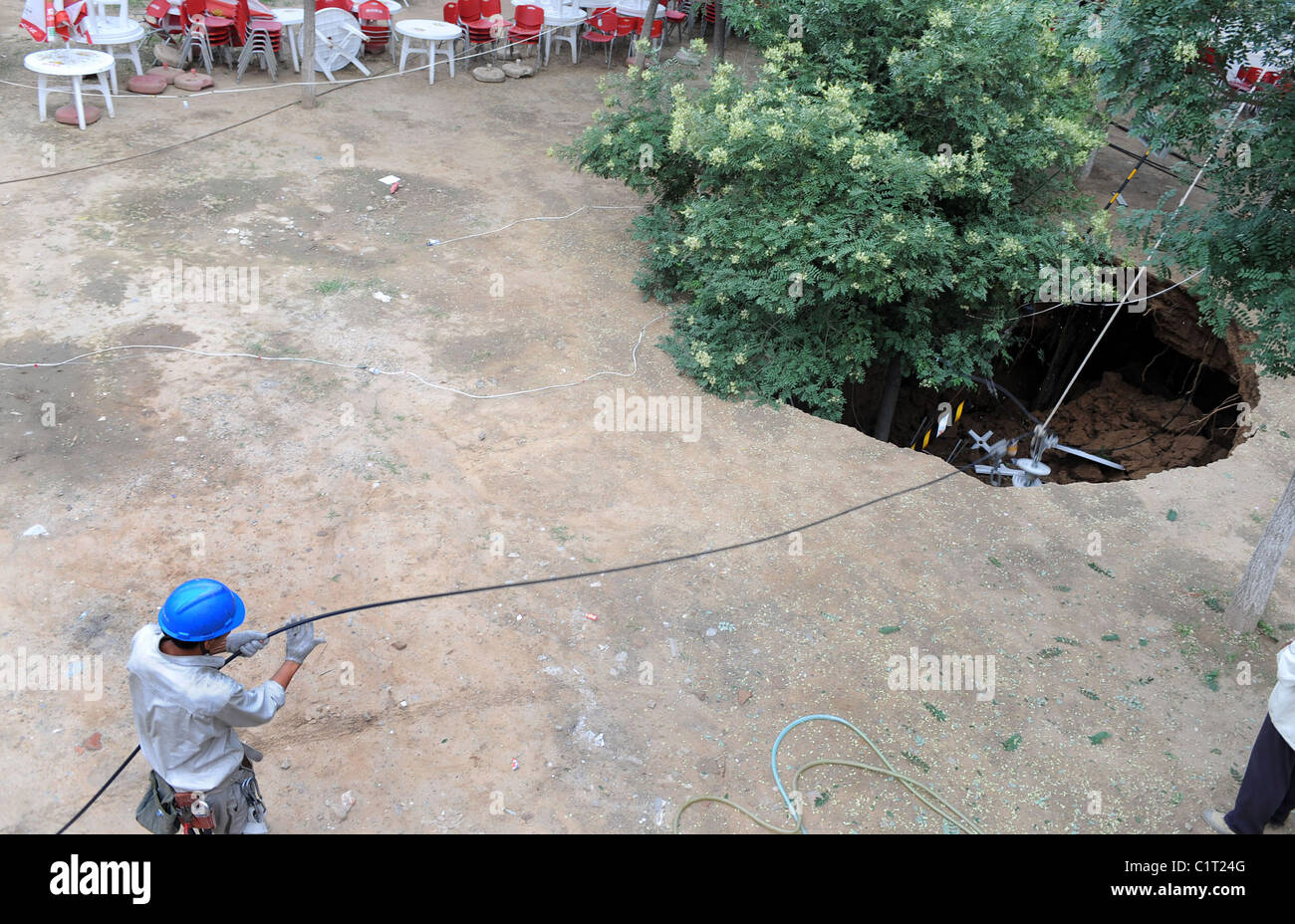Workers try to salvage a huge tree which has disappeared into a hole ...