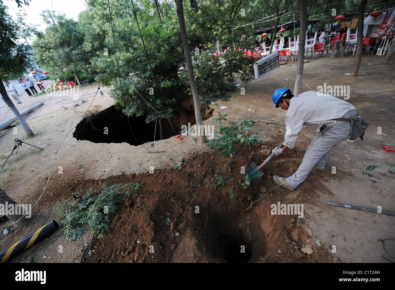 Workers try to salvage a huge tree which has disappeared into a hole ...
