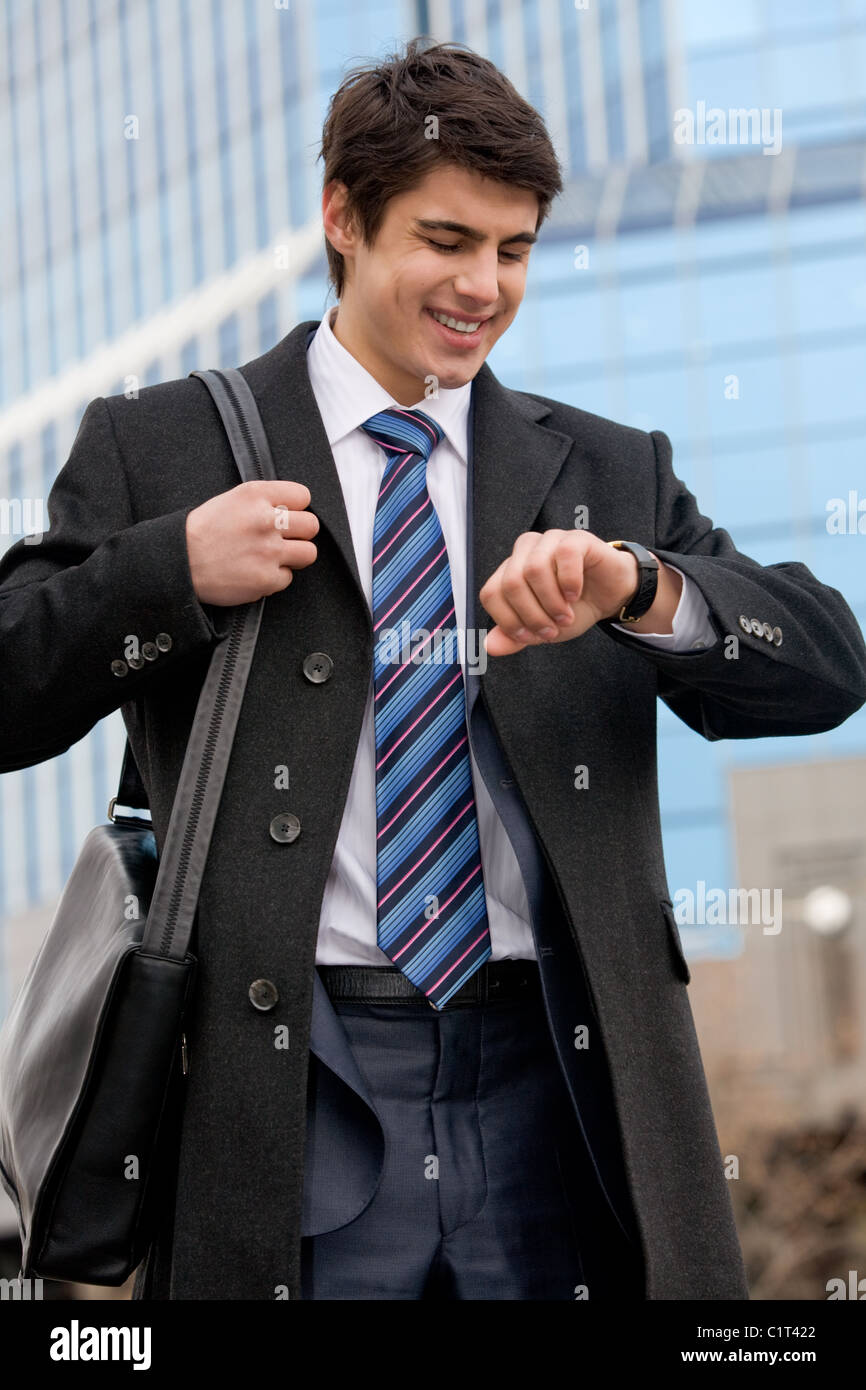Portrait of elegant businessman looking at his watch with office ...
