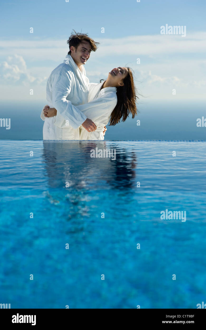 Couple embracing and laughing at edge of infinity pool, both wearing ...
