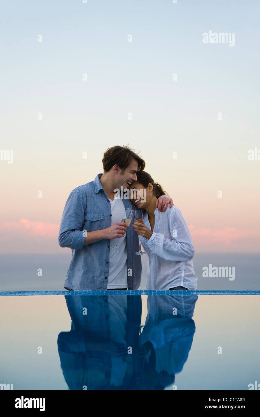 Couple embracing at edge of infinity pool, enjoying champagne Stock ...
