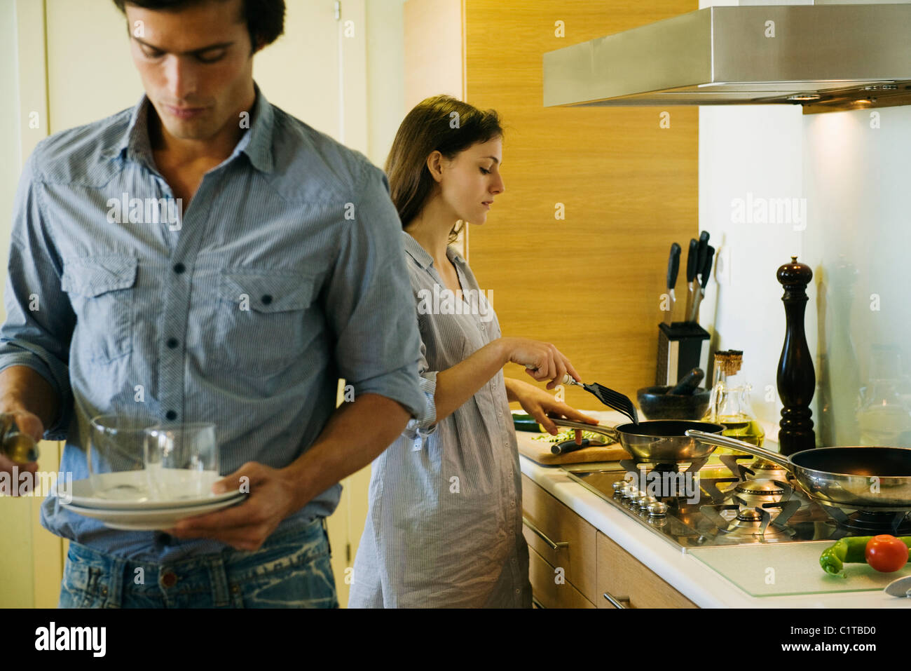Couple in kitchen, woman cooking while man sets table Stock Photo - Alamy