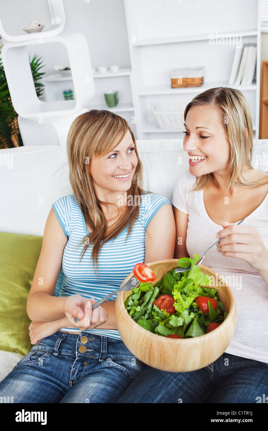 Two female friends eating salad together on a sofa Stock Photo - Alamy