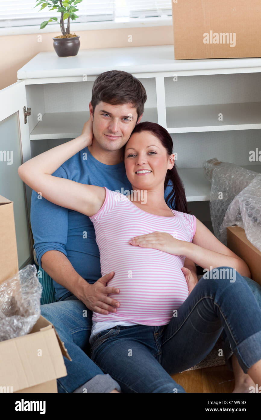 Happy couple in their new home sitting on the floor among cardboard ...