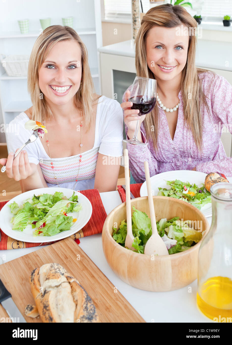 Two positive female friends eating salad in the kitchen Stock Photo - Alamy
