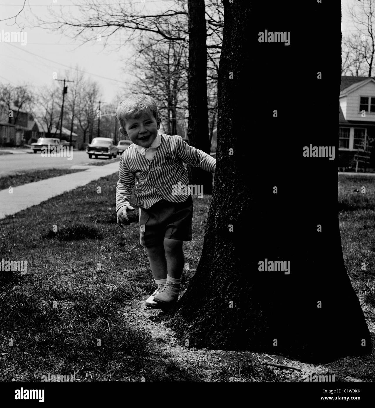 Boy standing near tree trunk and looking at camera Stock Photo - Alamy