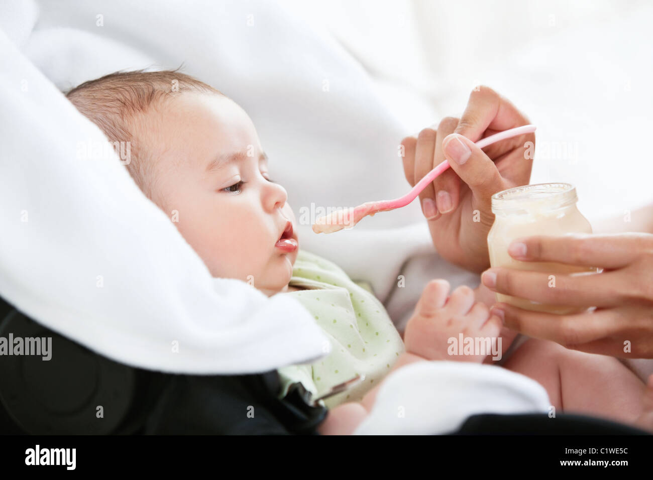 Close-up of a young mother giving mashed potatoes to her baby for lunch ...