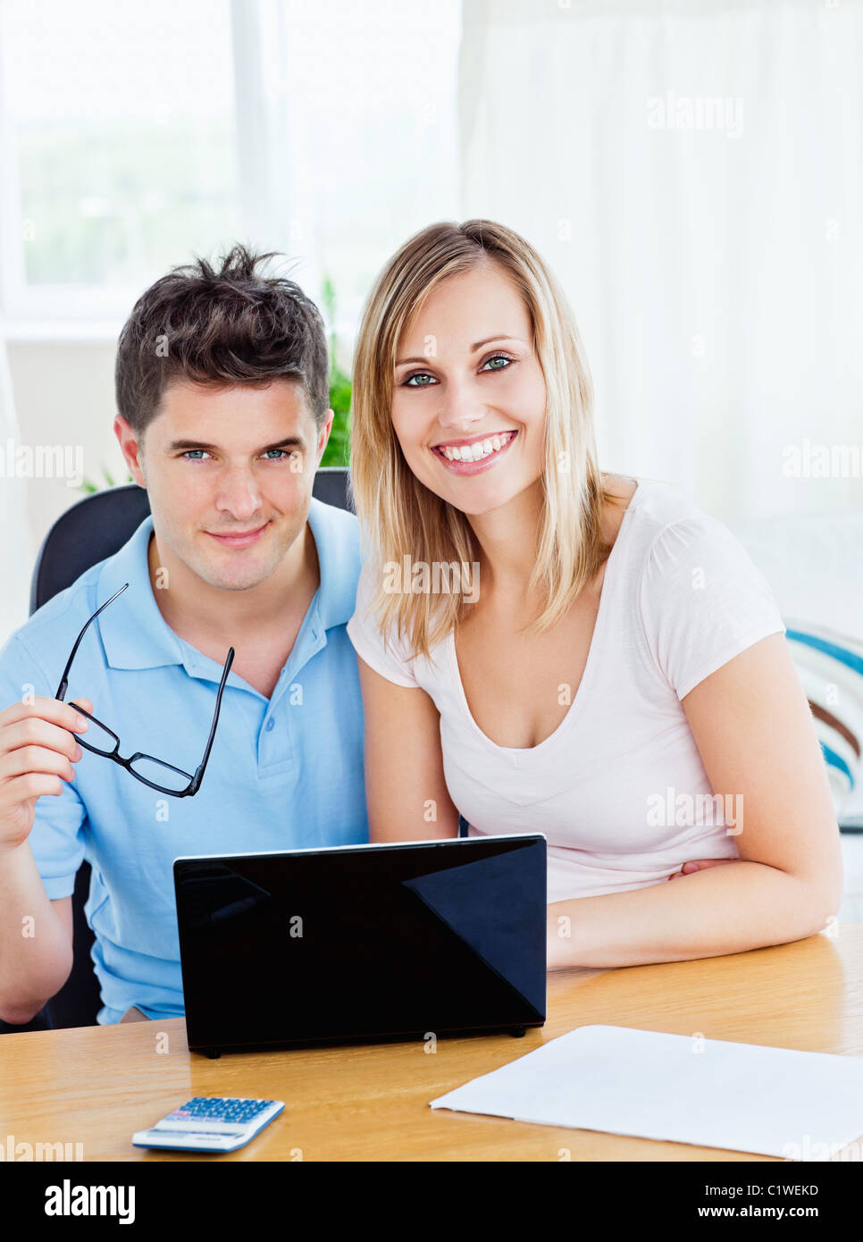 Portrait of a cheerful couple using a laptop sitting together at a ...