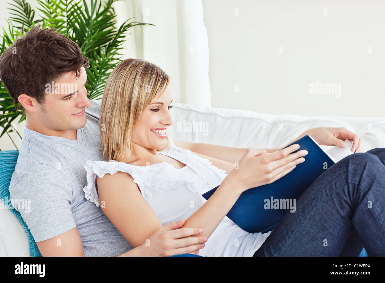 Cute couple browsing a book lying on the sofa Stock Photo - Alamy