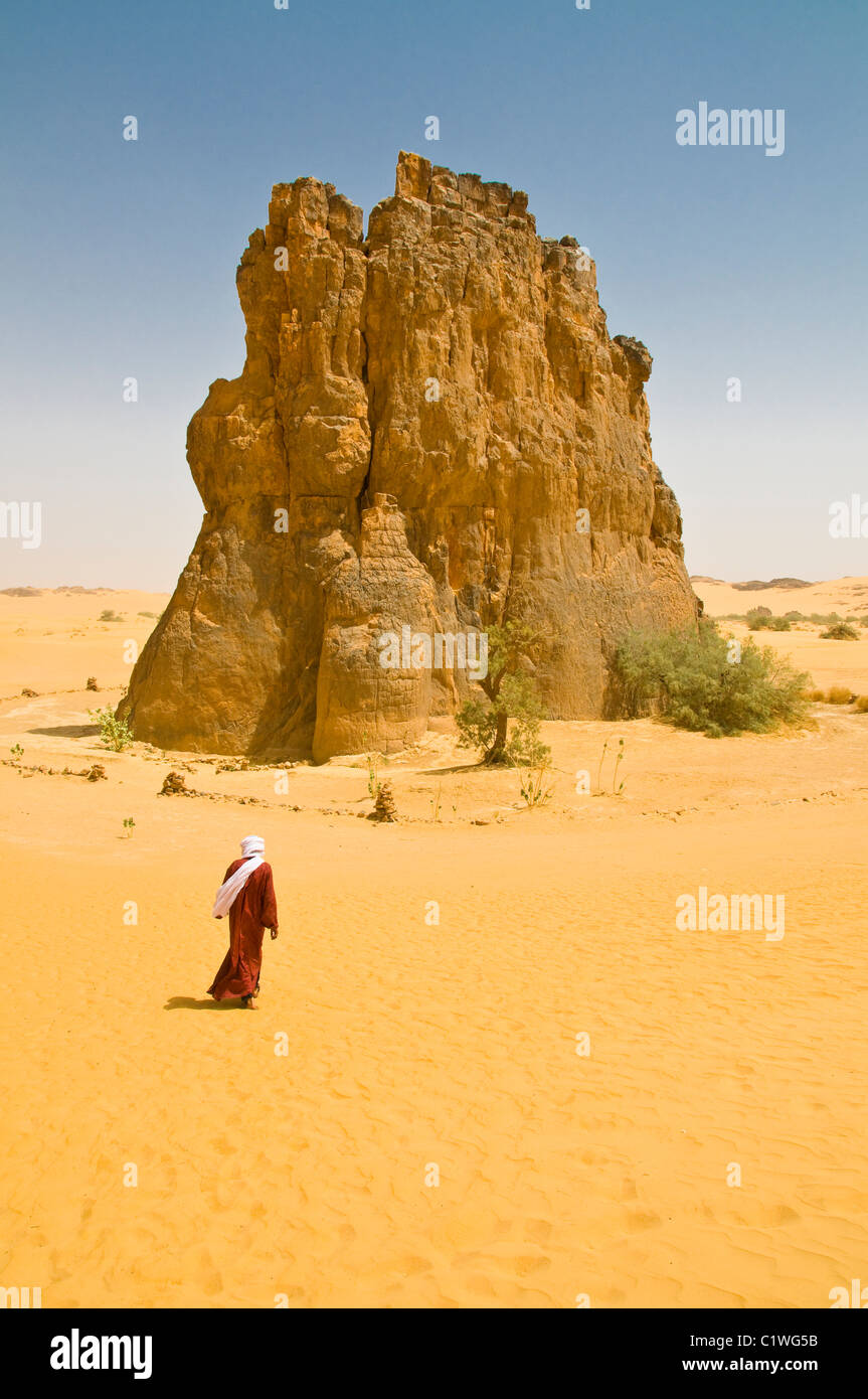Algeria, Sahara desert, Man walking towards rock in sand Stock Photo ...