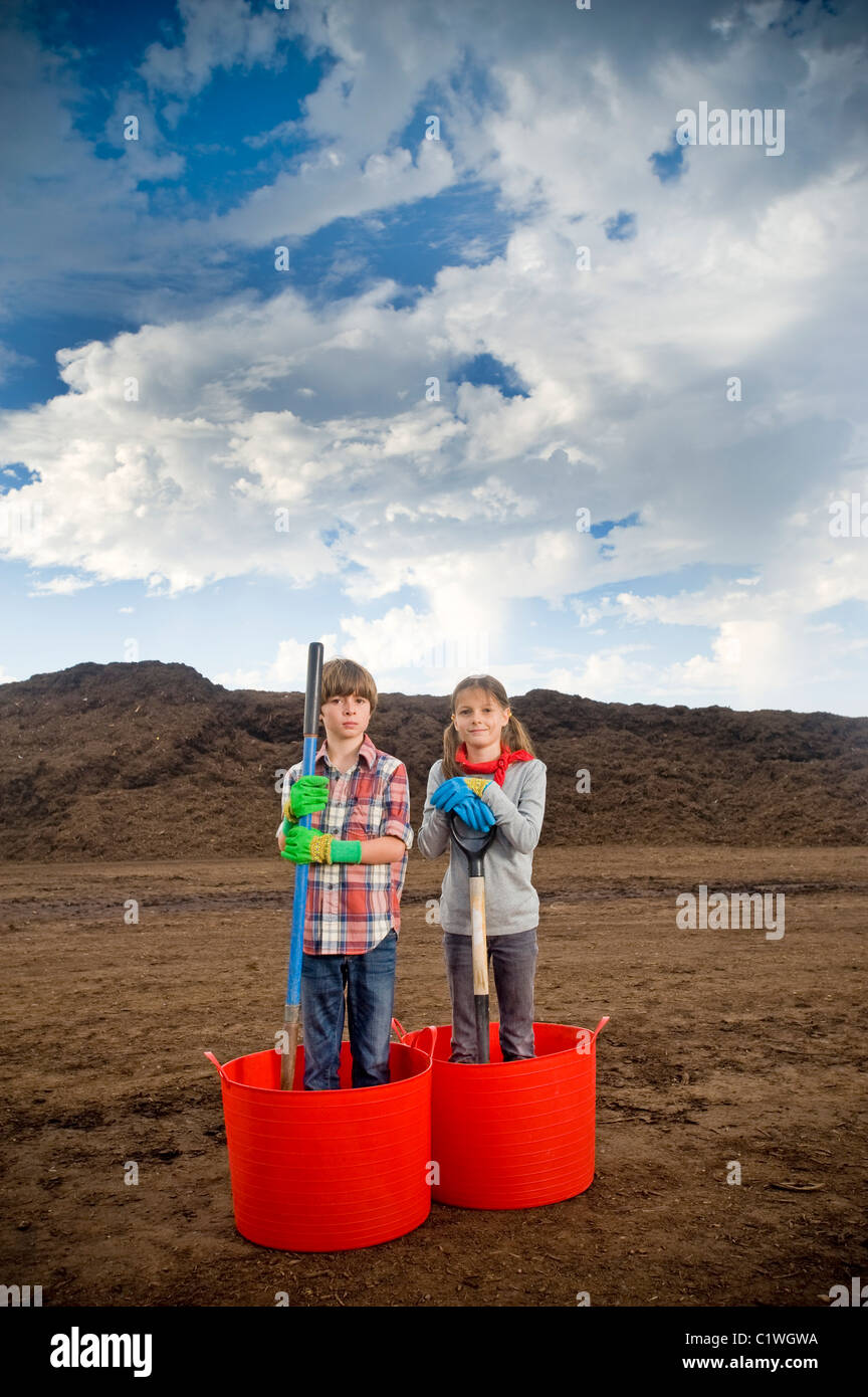 Boy and a girl standing in buckets with a mountain of compost in the ...