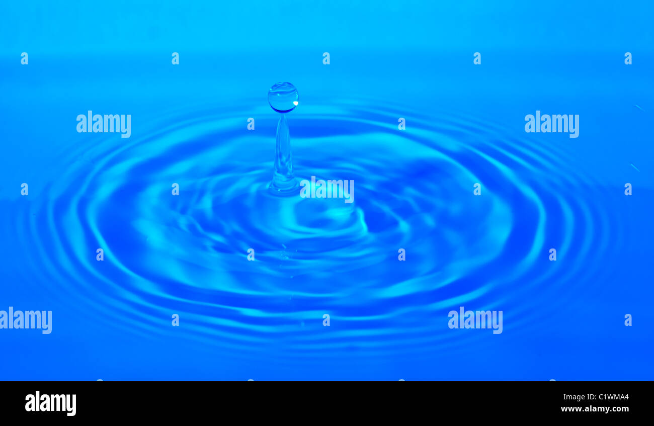 A single droplet of water splashing into more water creating a ripple ...