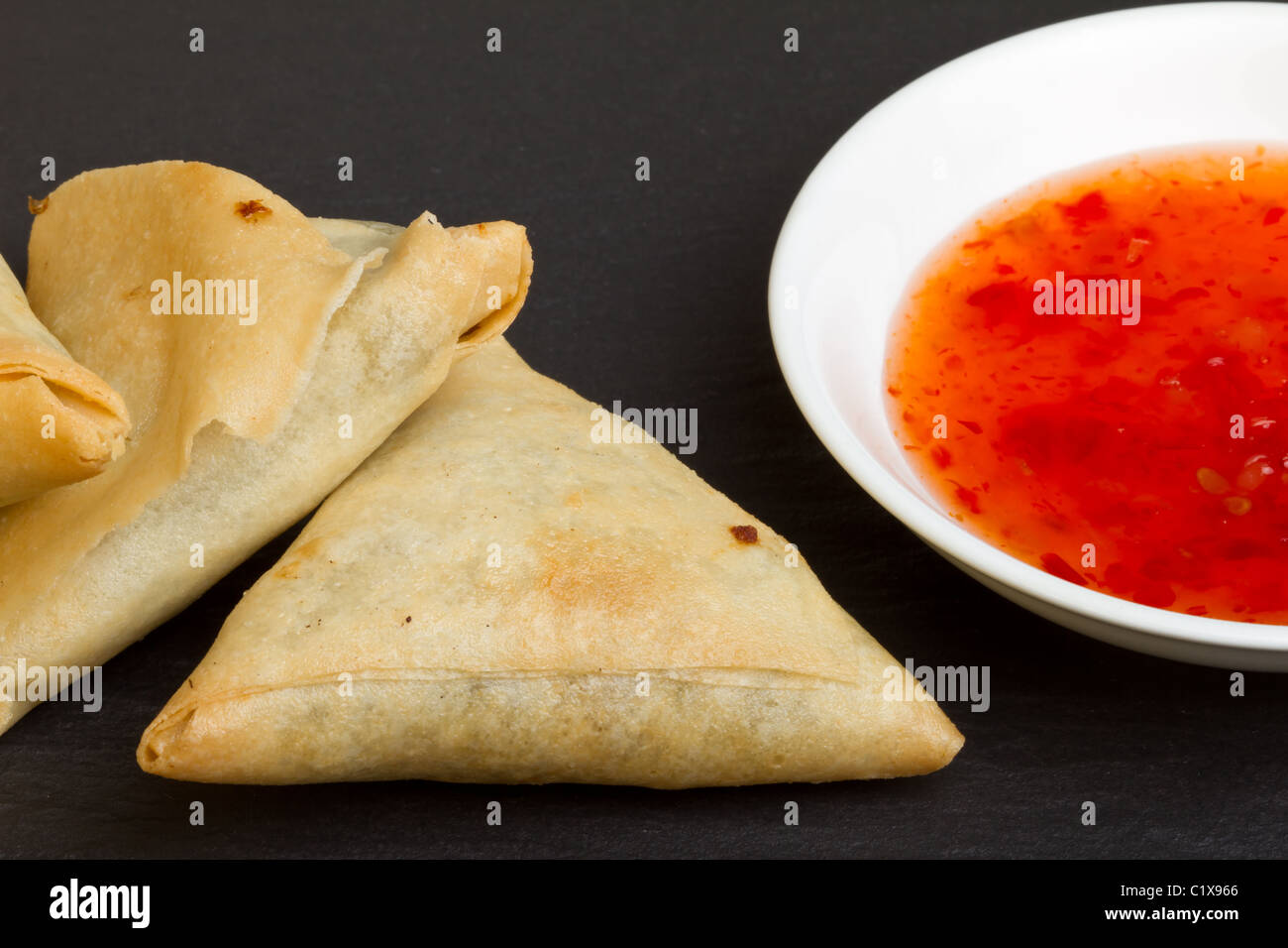 Sweet chilli dipping sauce and golden fried samosa's on dark slate ...