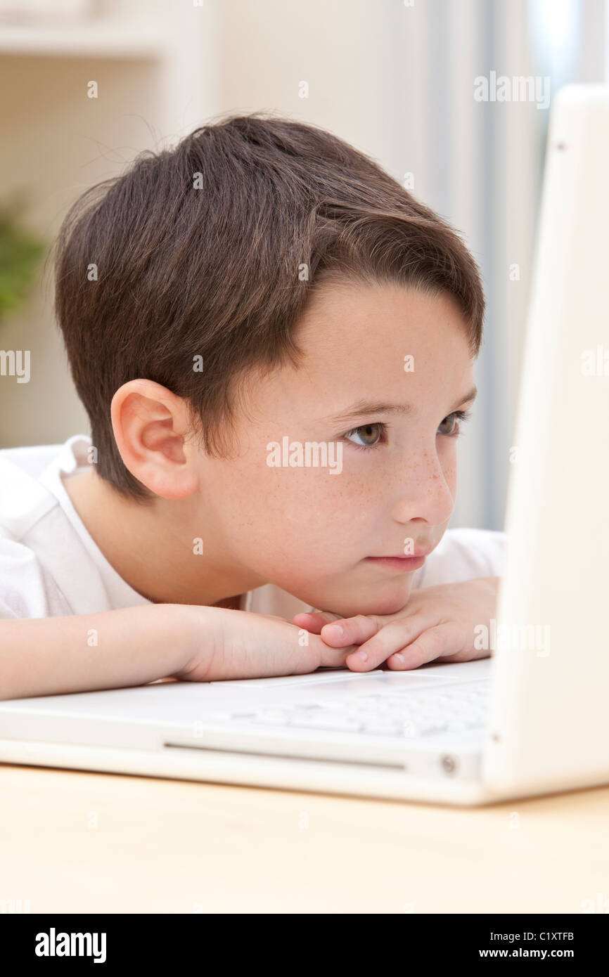 A young boy child resting on his hands and looking at the screen while ...