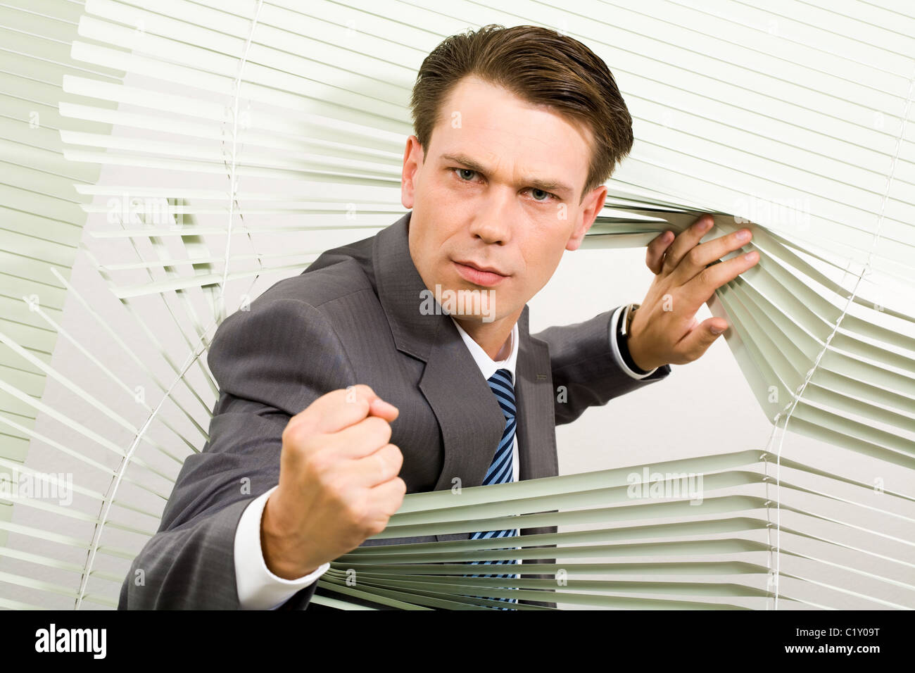 Portrait of angry man looking at camera out of venetian blind and ...