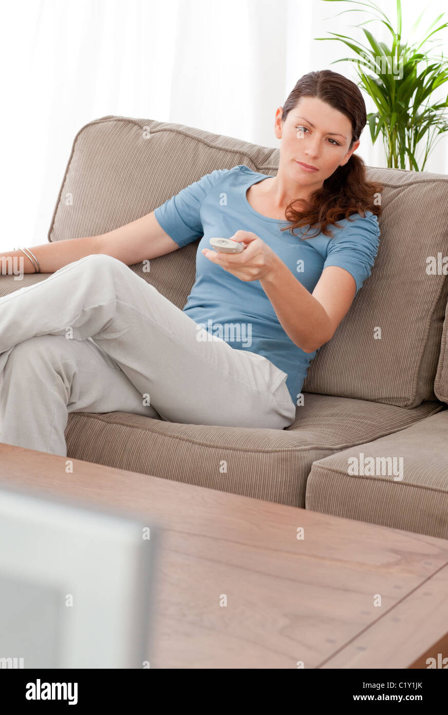 Serious woman changing channel while relaxing in the living-room Stock ...