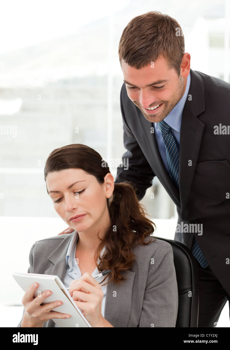 Serious businesswoman taking notes while discussing with her colleague ...