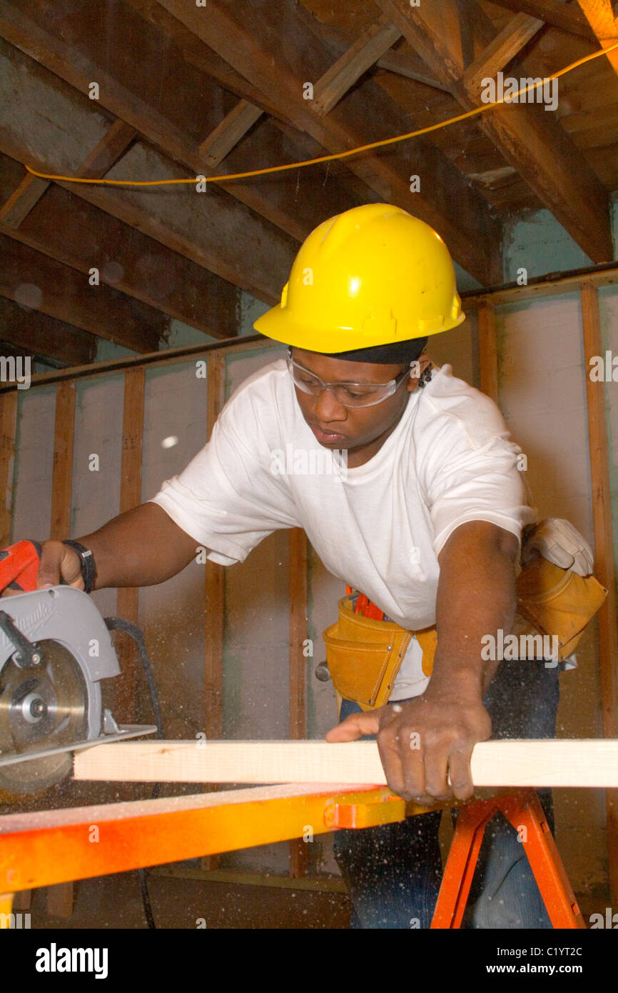 Black teen volunteer carpenter cutting board with circular saw for ...