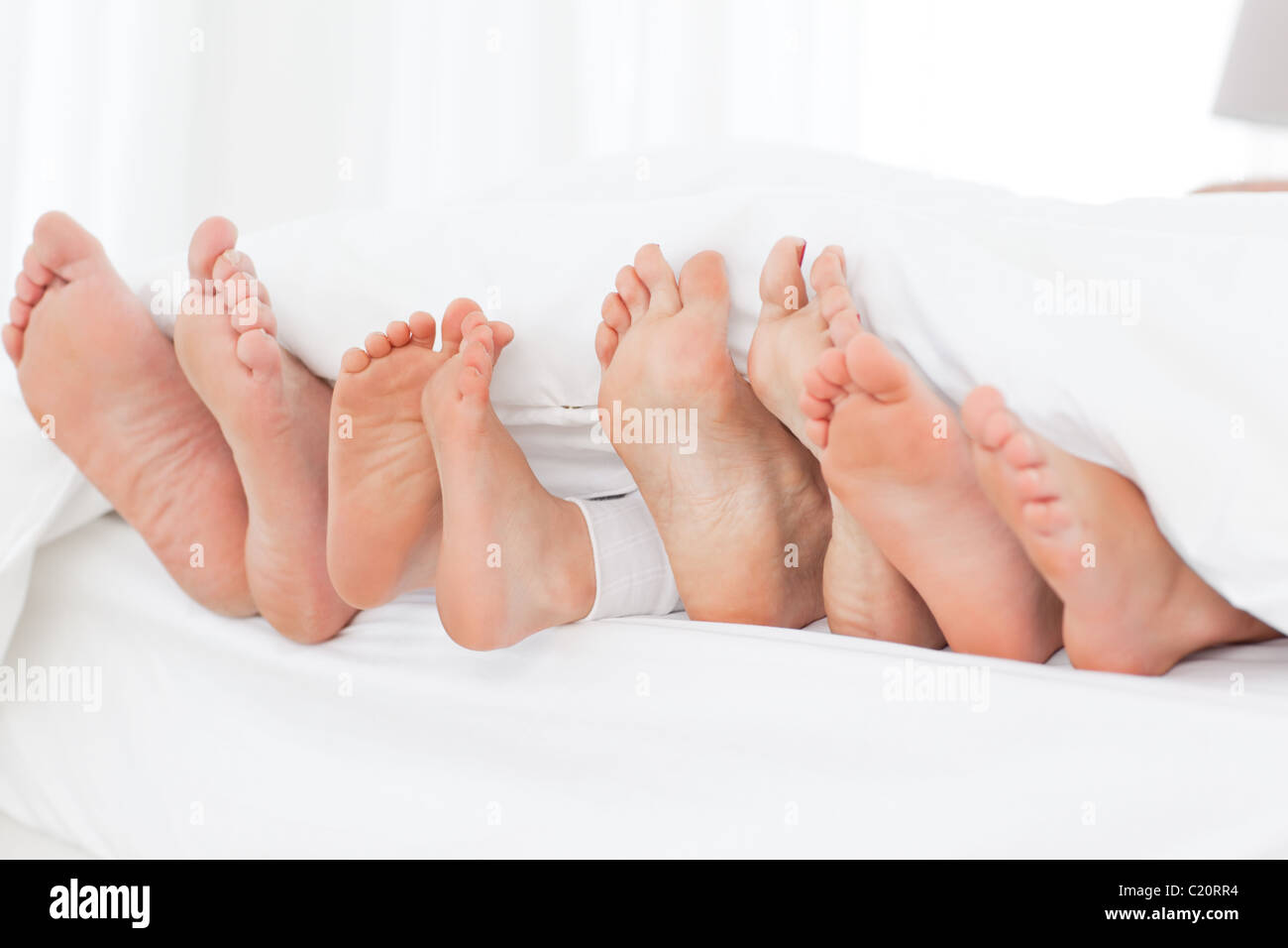 Whole family showing their feet while lying on a bed Stock Photo - Alamy