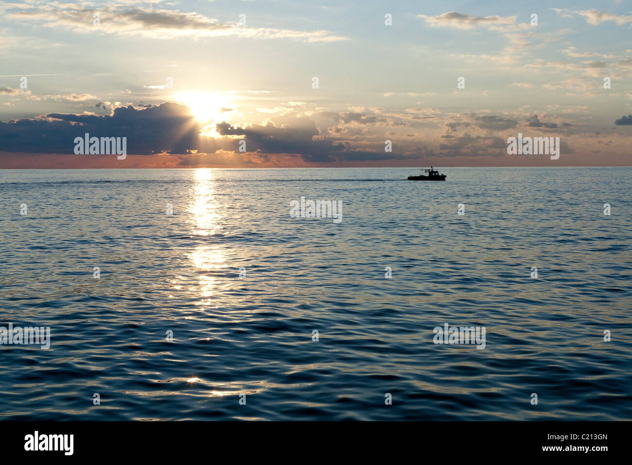 Small boat sailing on the sea at sunset and clouds Stock Photo - Alamy
