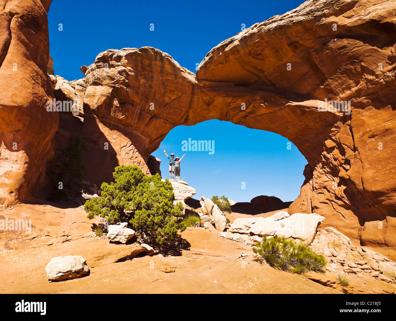 A man and woman stand together on a rock below Broken Arch posing for ...