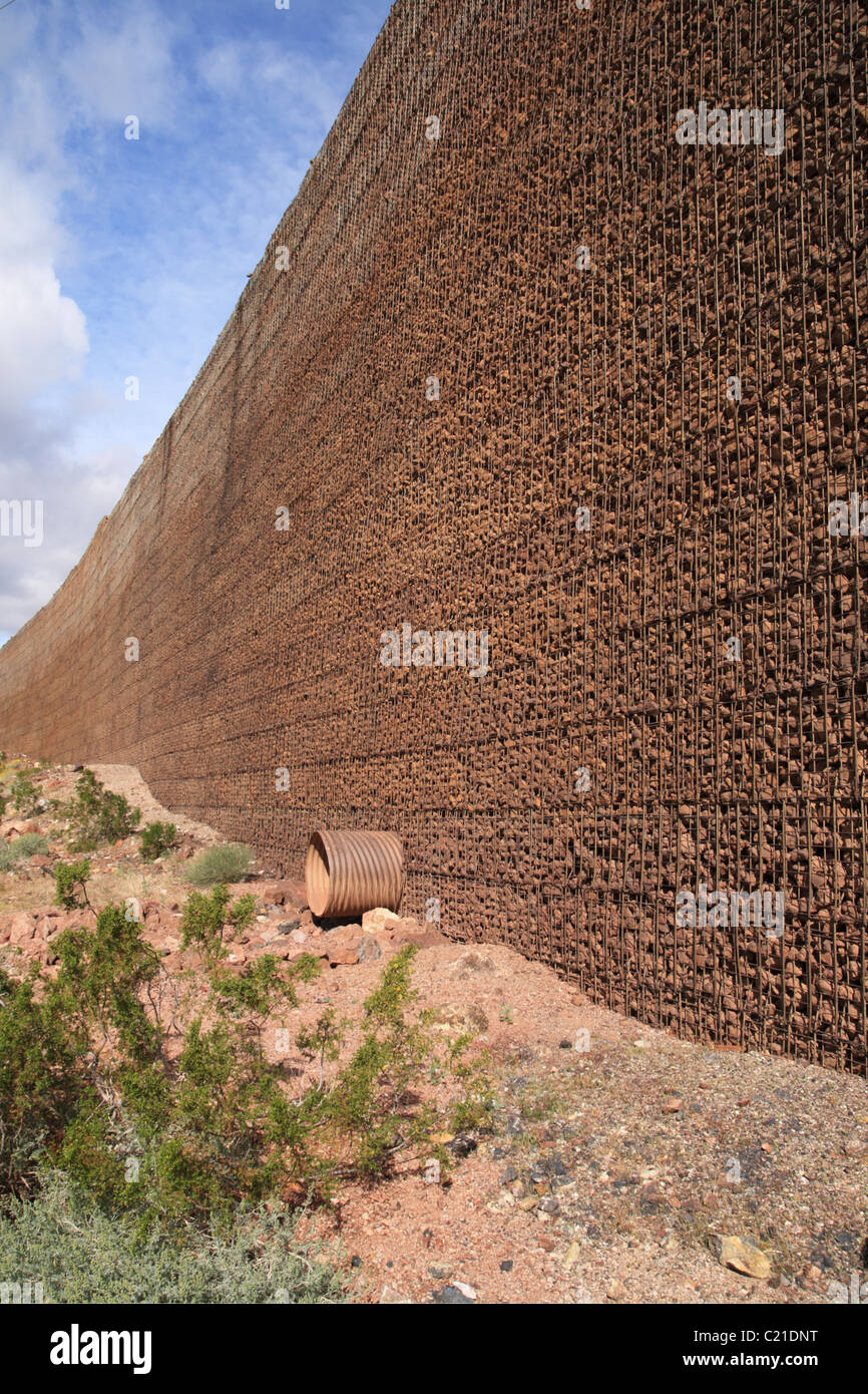 vertical image of a wire mesh and loose rock retaining wall with drain ...