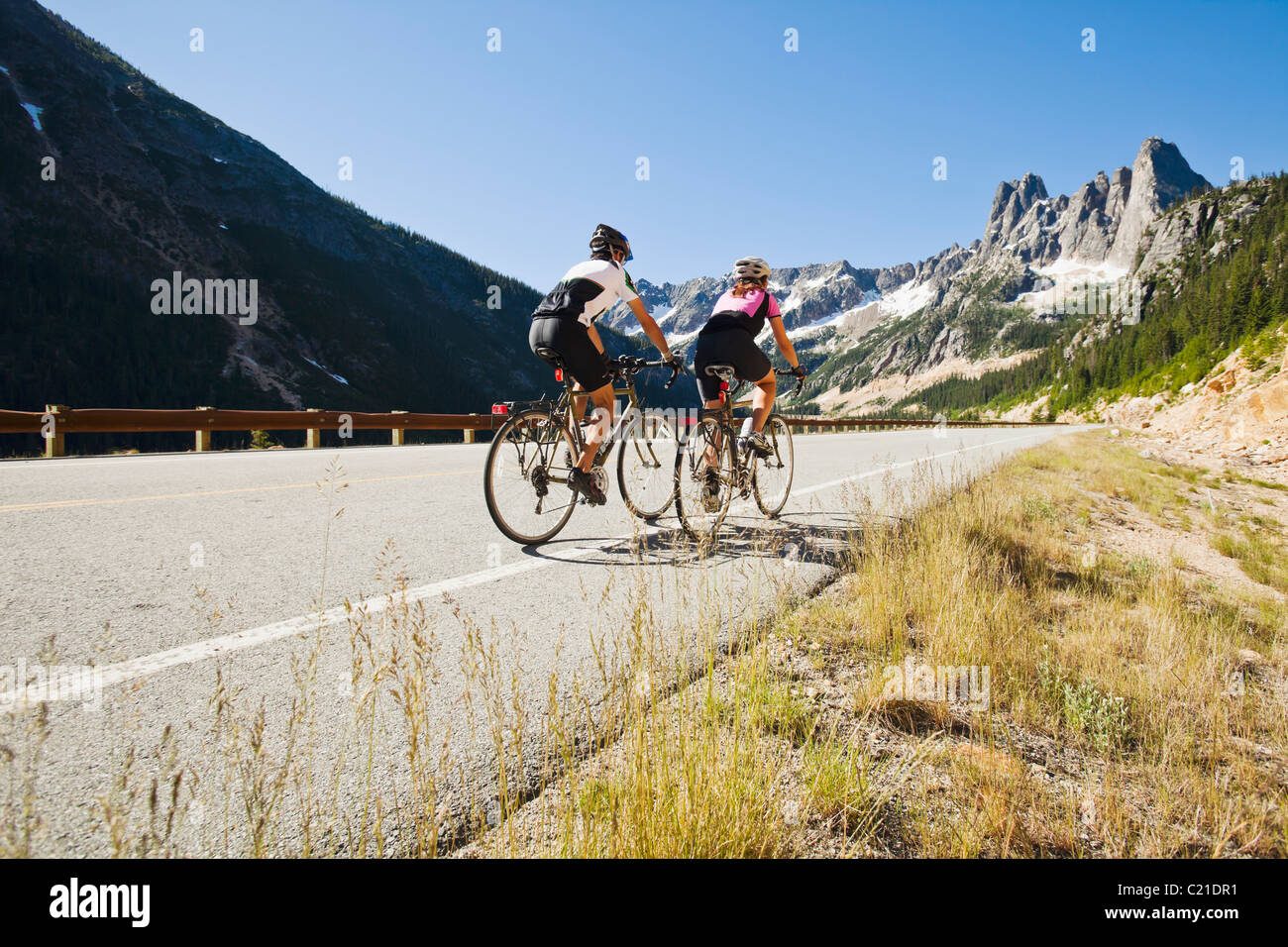 A young couple rides bikes up a mountain pass. North Cascades of ...