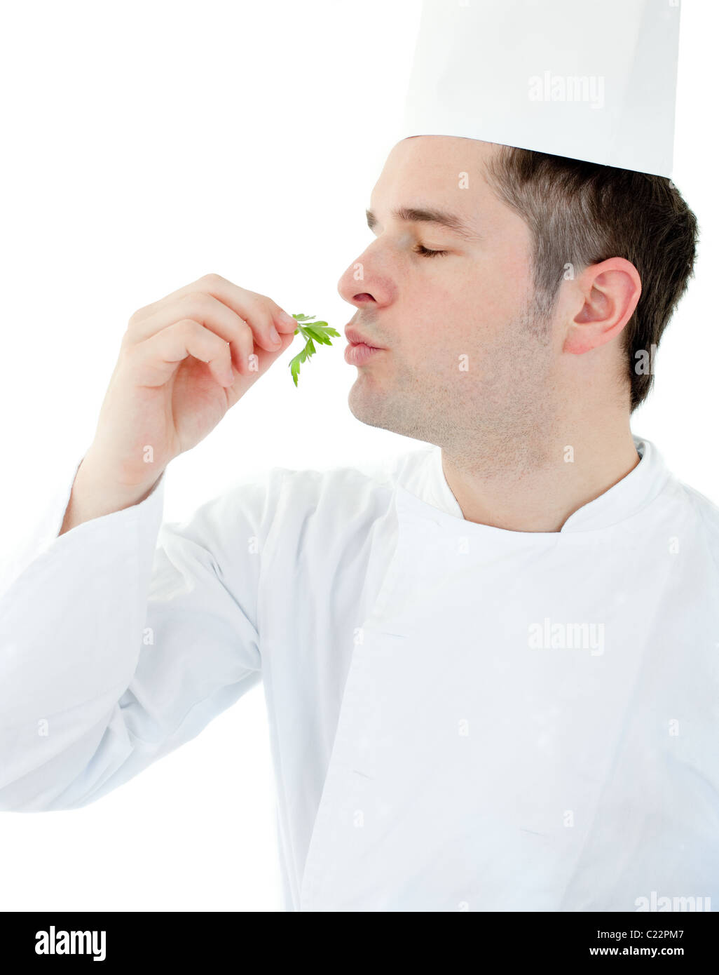 Charming young cook with closed eyes holding a herb against white ...