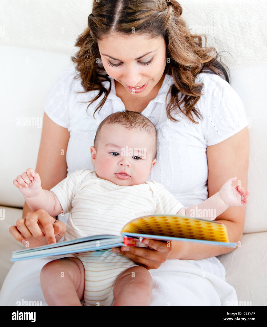 Loving mother reading a story to her adorable baby sitting on the sofa ...