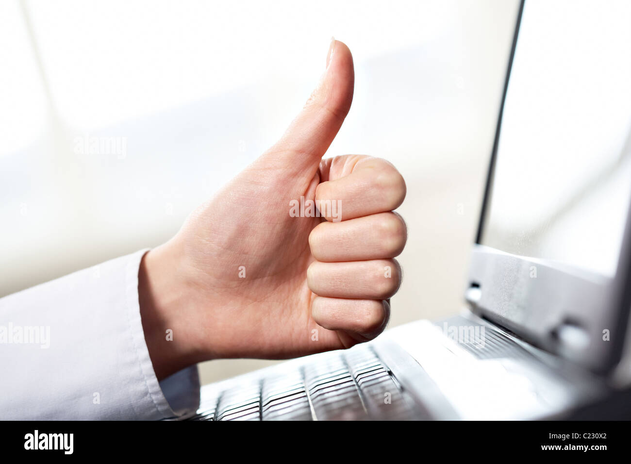 Close-up of female hand keeping thumb up over laptop screen on ...