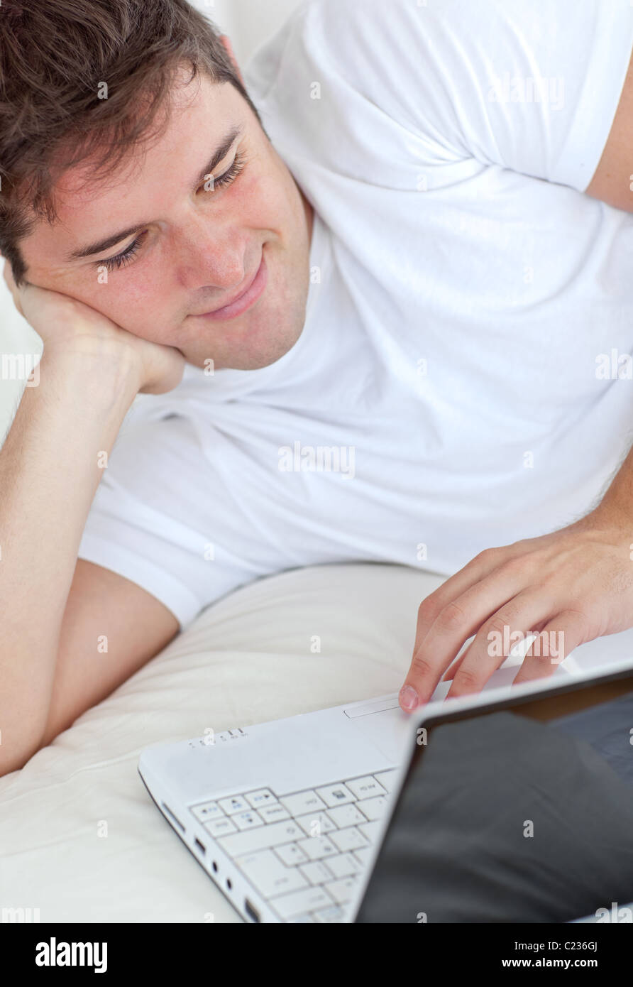 Smiling man using his laptop lying on his bed Stock Photo - Alamy