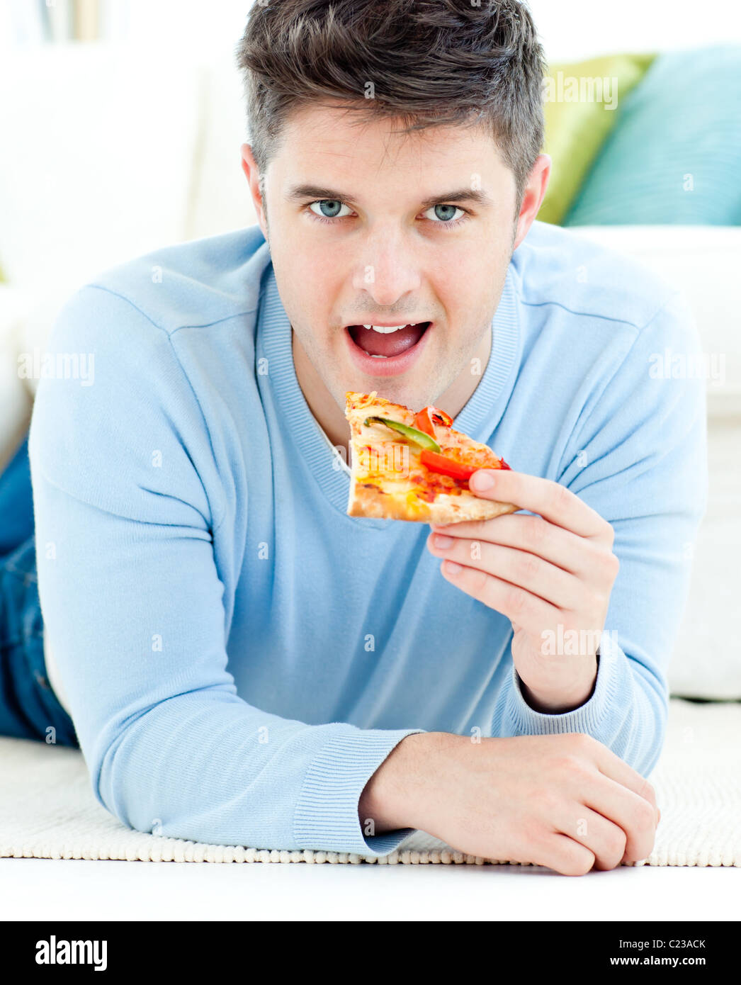 Young man lying on the ground and eating pizza Stock Photo - Alamy