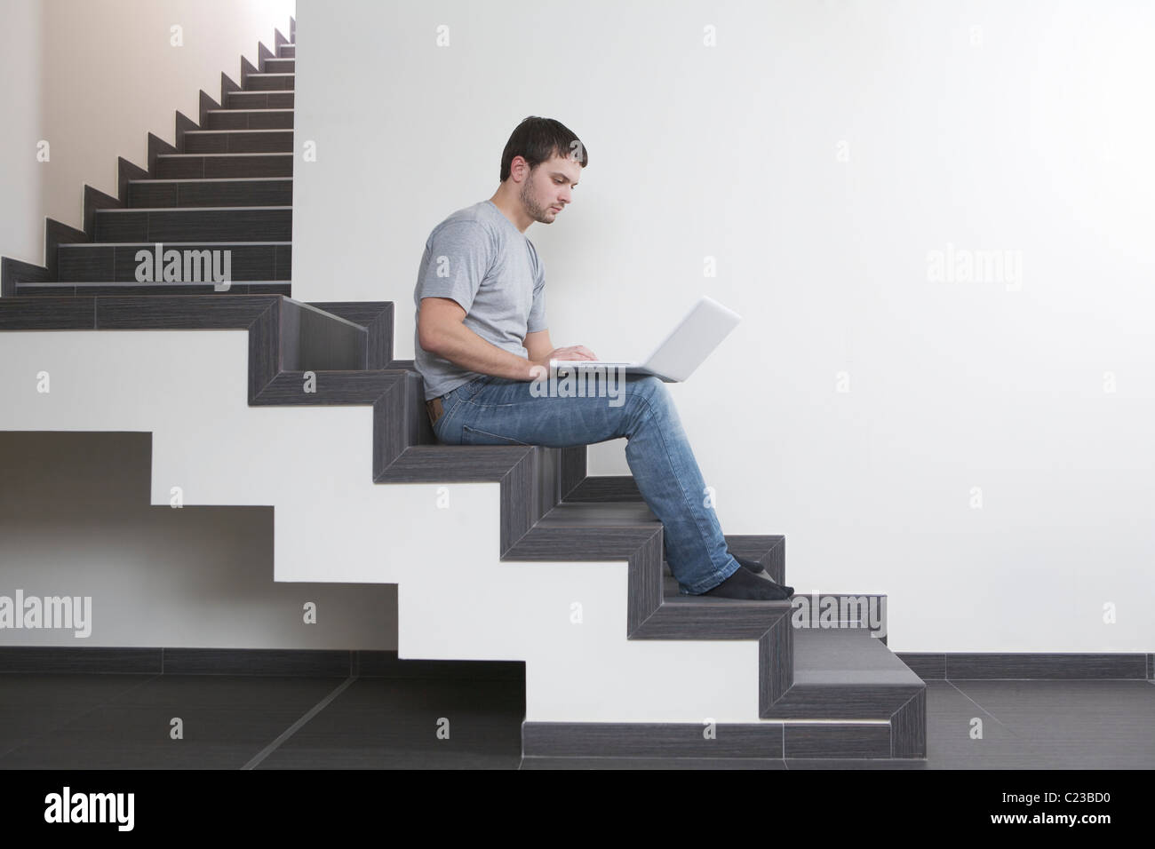 Young man sits on staircase with laptop Stock Photo - Alamy