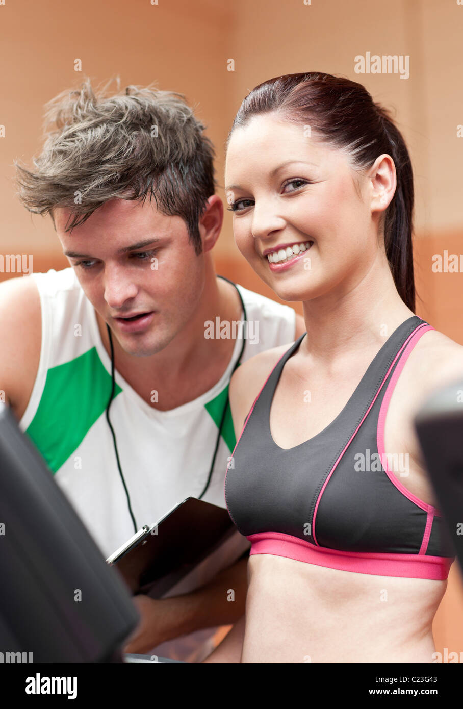 Cheerful female athlete standing on a running machine with her personal ...