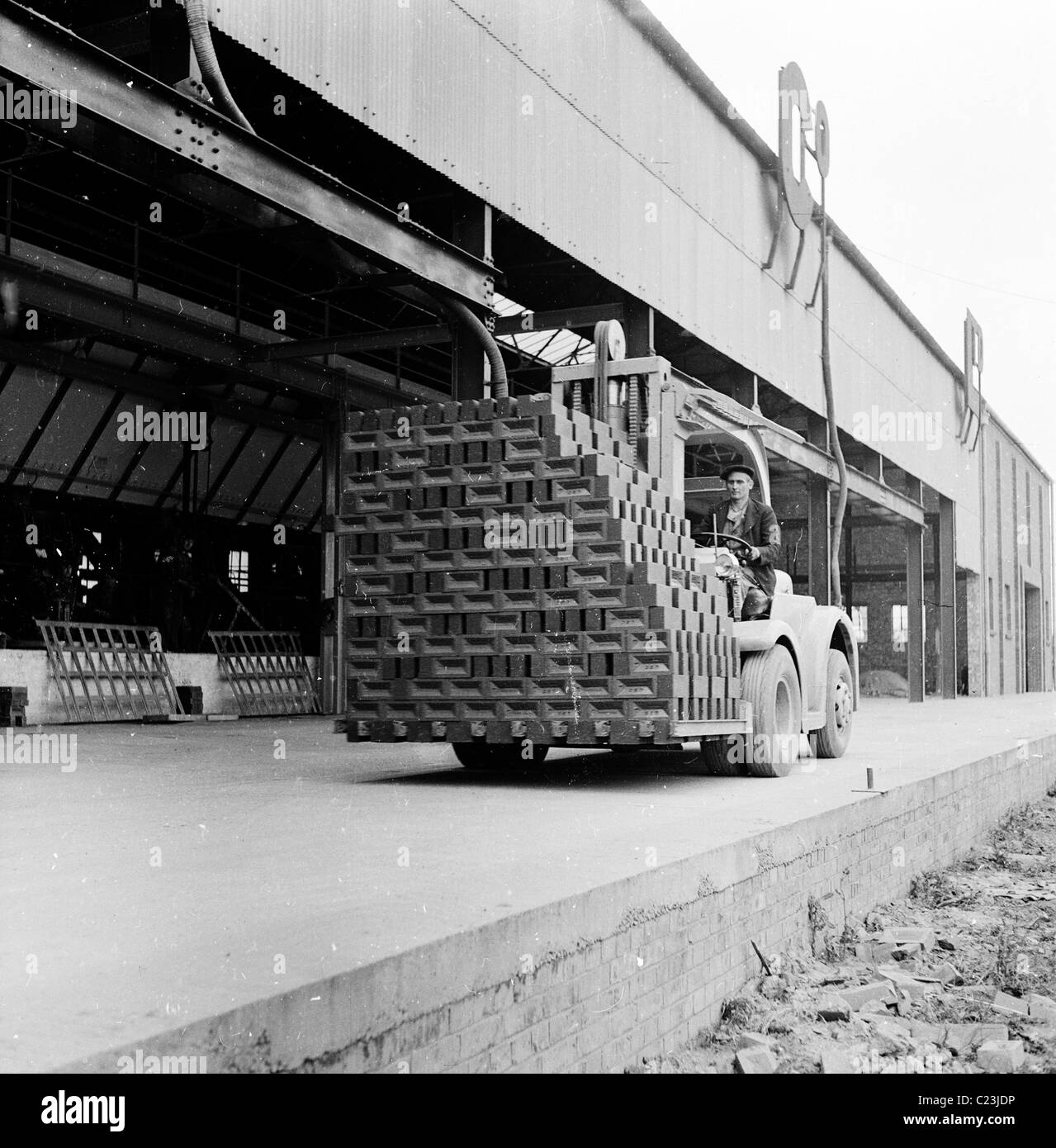 England, 1950s. Worker on a fork-lift truck removing bricks from the ...