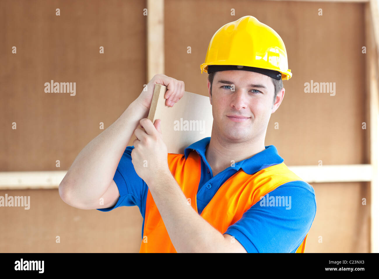 Confident young male worker with a yellow helmet carrying a wooden ...