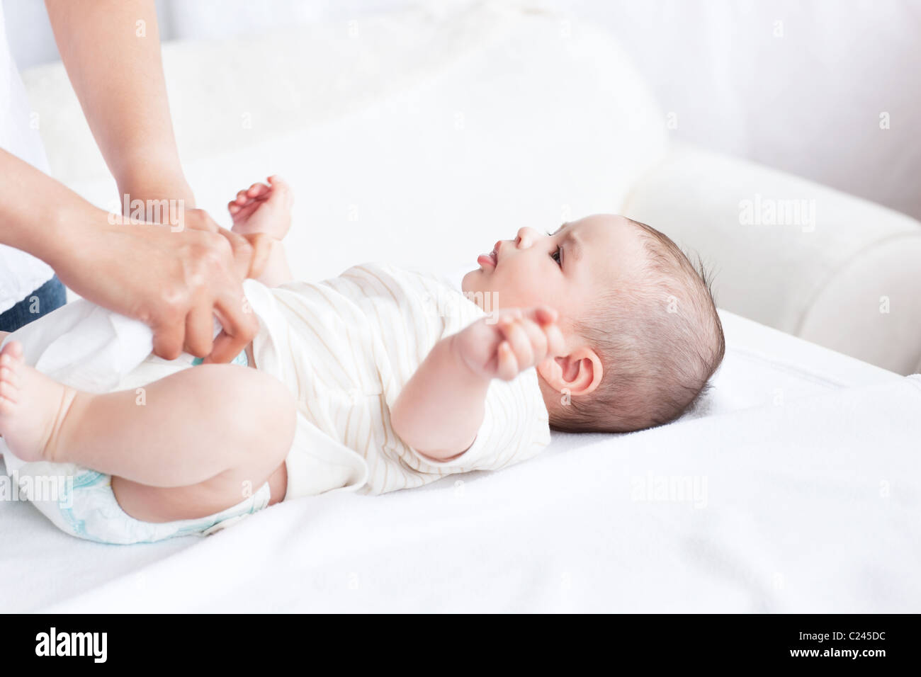 Close-up of a young mother changing the nappy of her baby lying on a ...