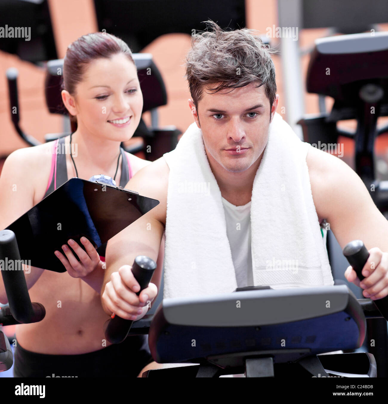 Smart female coach taking notes while her pupil is pedaling on a ...