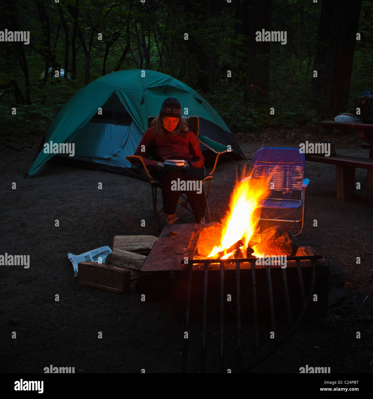 A middle aged woman sitting reading a book next to a camp fire Stock ...