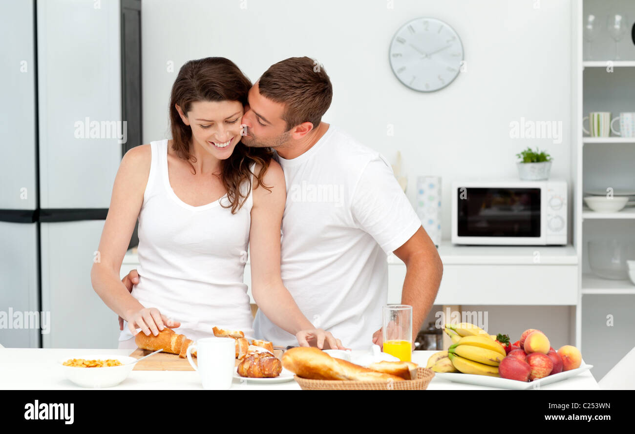 Affectionate man kissing his girlfriend while cutting bread for ...