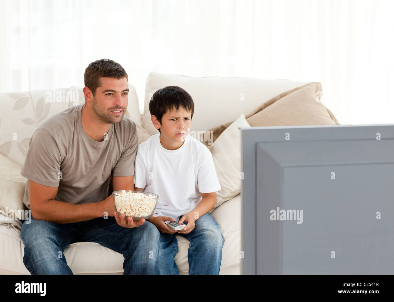 Concentrated father and son watching television while eating pop corn ...
