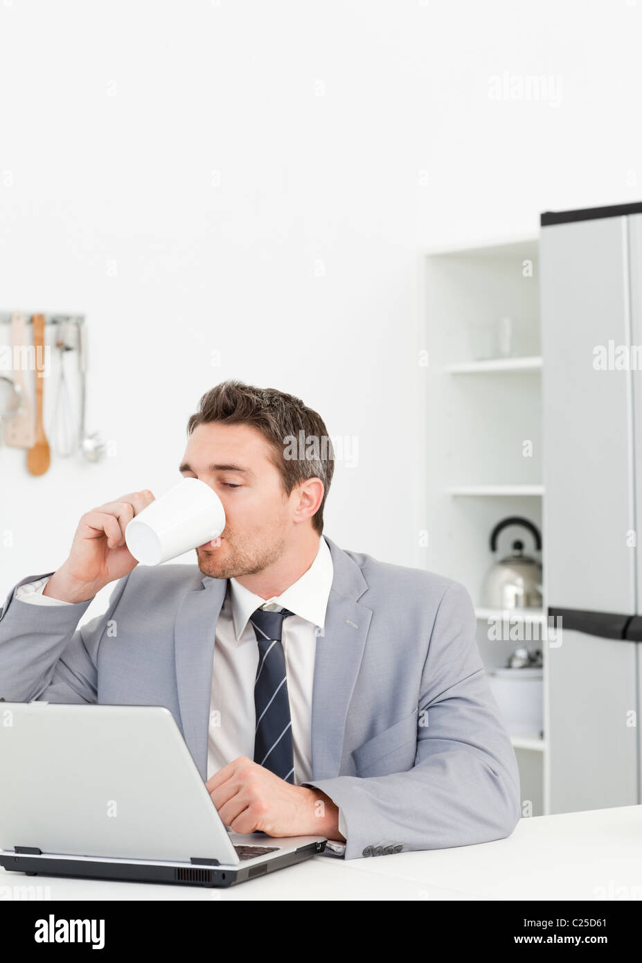 Businessman drinking while he is looking at his laptop Stock Photo - Alamy