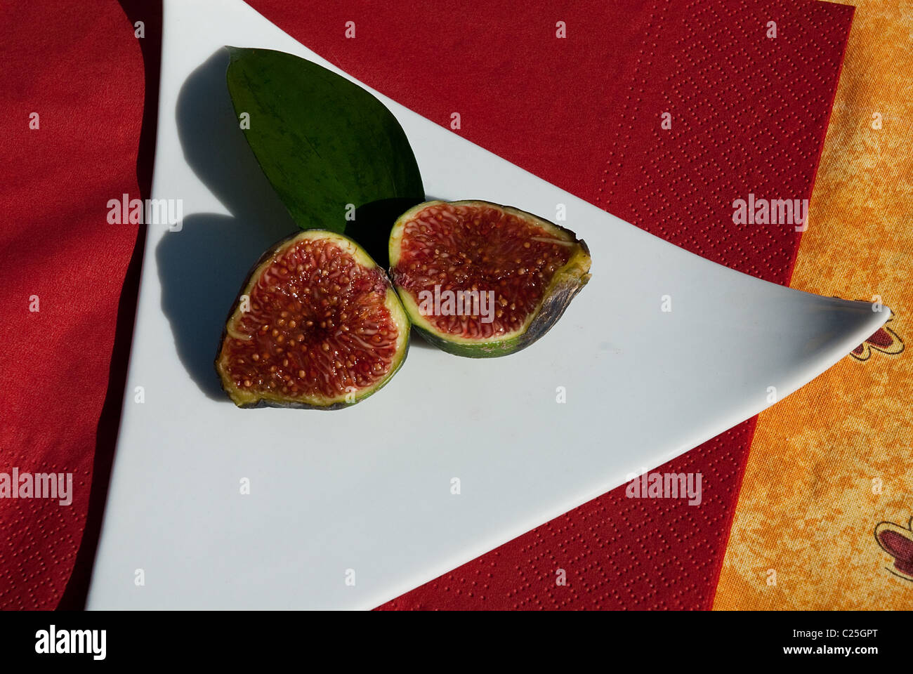 A fig split in two with a fig leaf behind, set on a triangular white ...