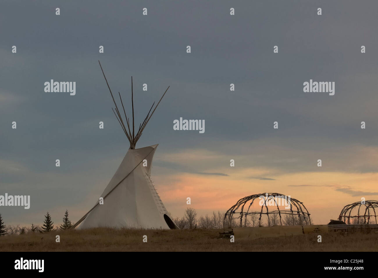 A Native American Teepee at dusk with a drying rack outside of the tee ...