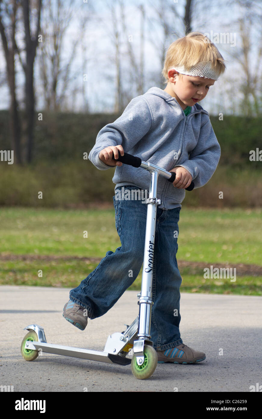 A young child blond boy on a scooter in park with injured head ...
