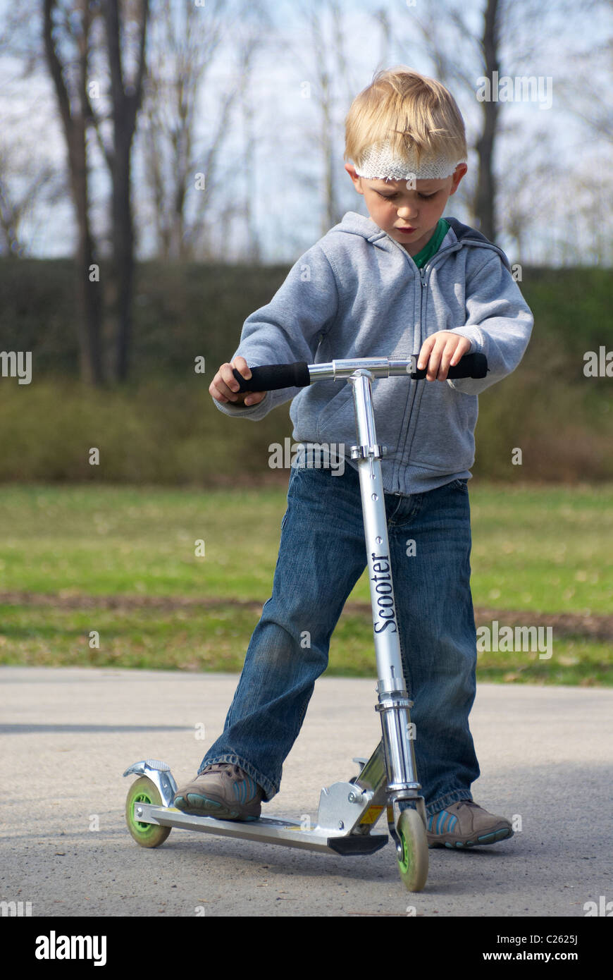 A young child blond boy on a scooter in park with injured head ...