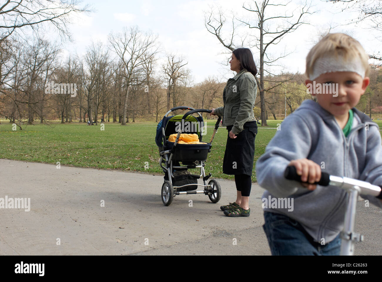 A young child blond boy on a scooter in park with injured head ...