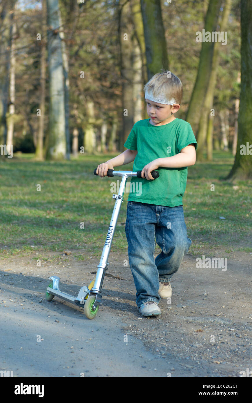 A young child blond boy on a scooter in park with injured head ...